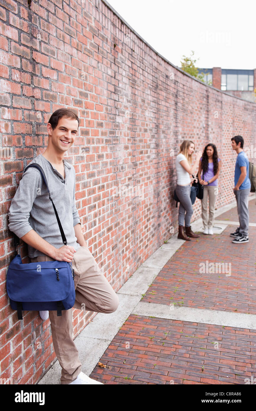 Portrait of a male student leaning on a wall while his friends are ...