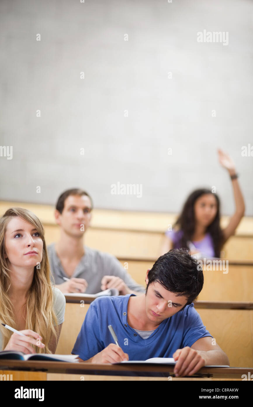Portrait of students taking notes while their classmate is raising her ...