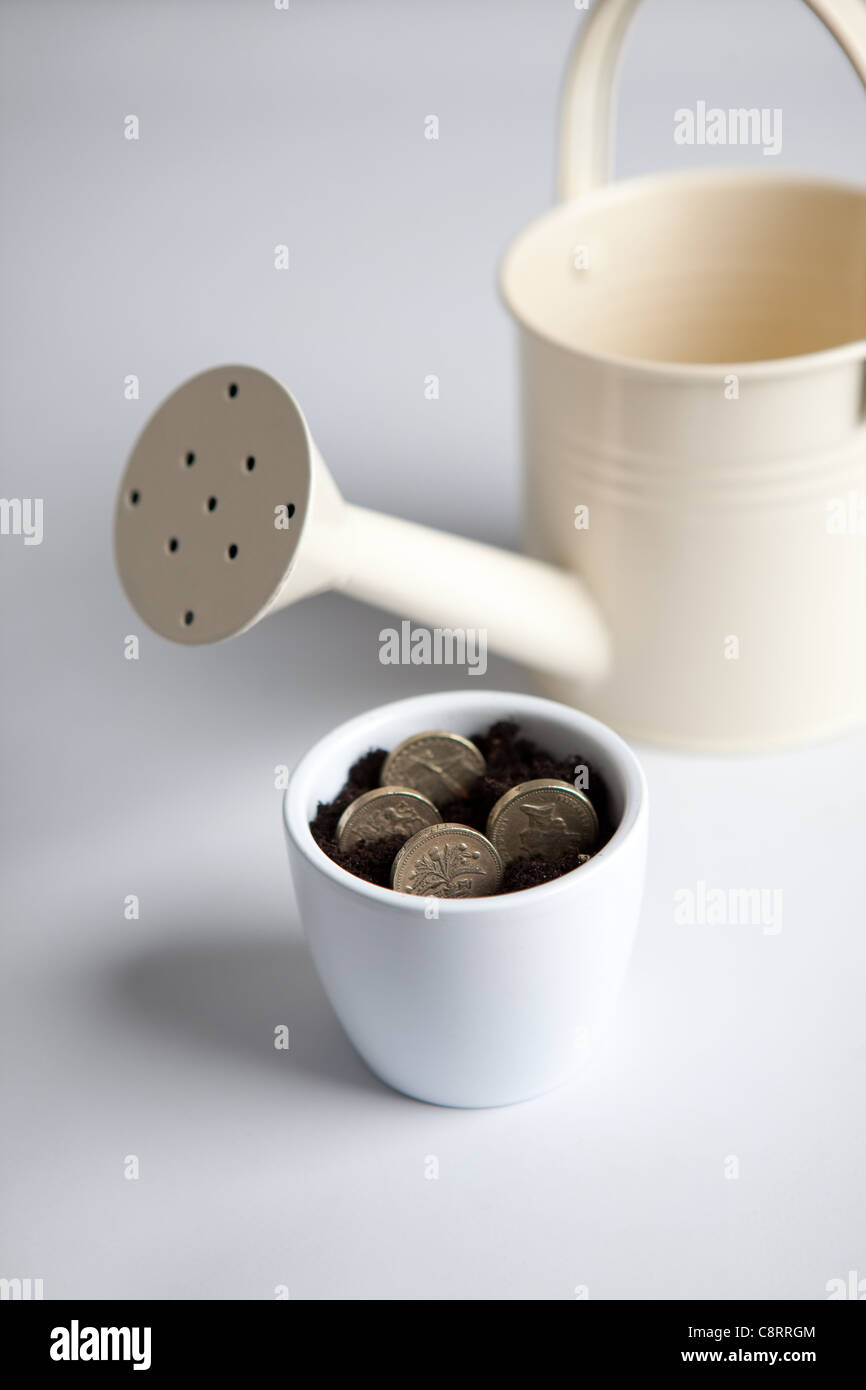 A plant pot holding pound coins beside a watering can, to give a ...