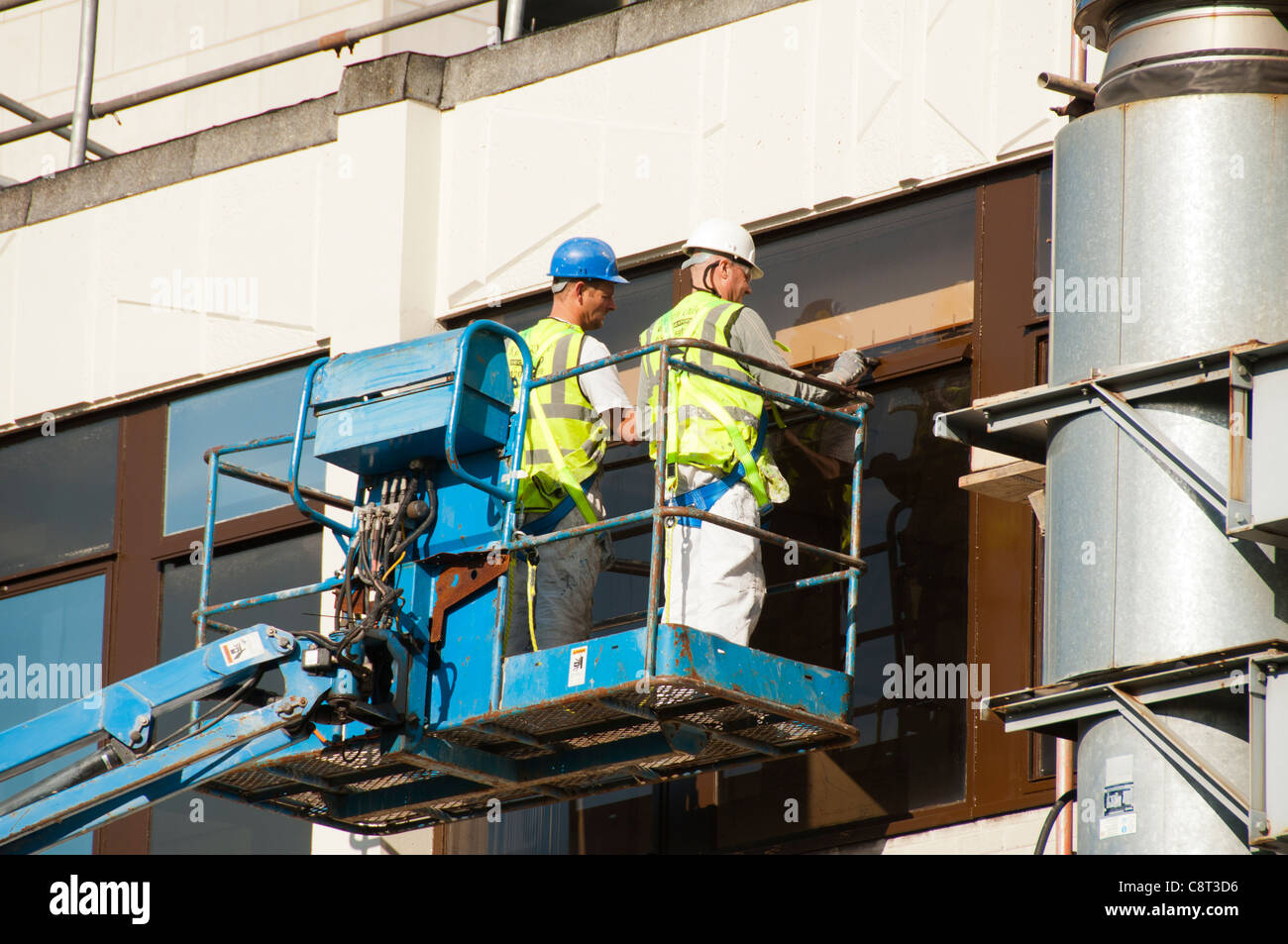 Two workmen on an access platform painting office window frames ...