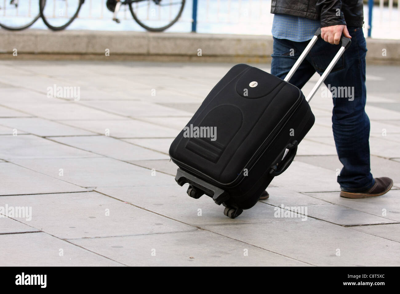 a male pulling a wheeled suitcase along The embankment of the River ...