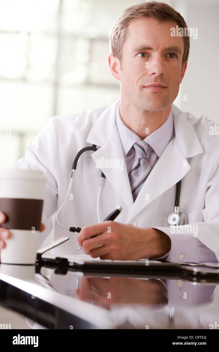 Caucasian doctor drinking coffee and writing in medical record Stock ...