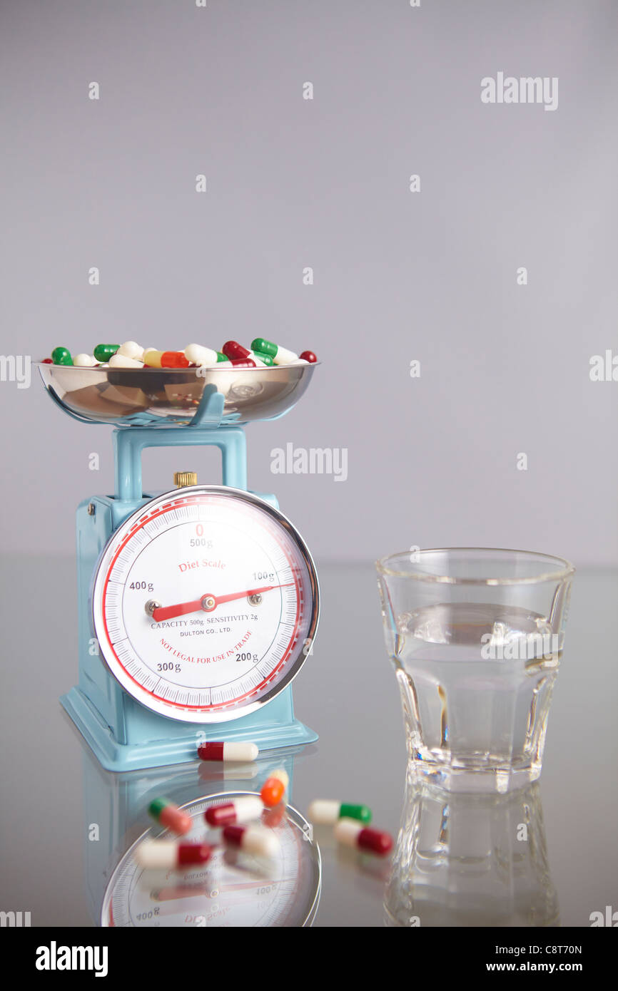 Pills on weight scale along with glass of water Stock Photo - Alamy