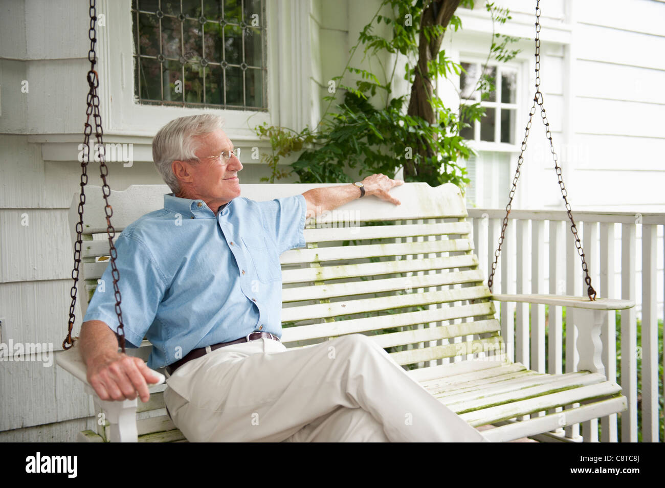 USA, New York State, Old Westbury, Senior man sitting on porch swing ...