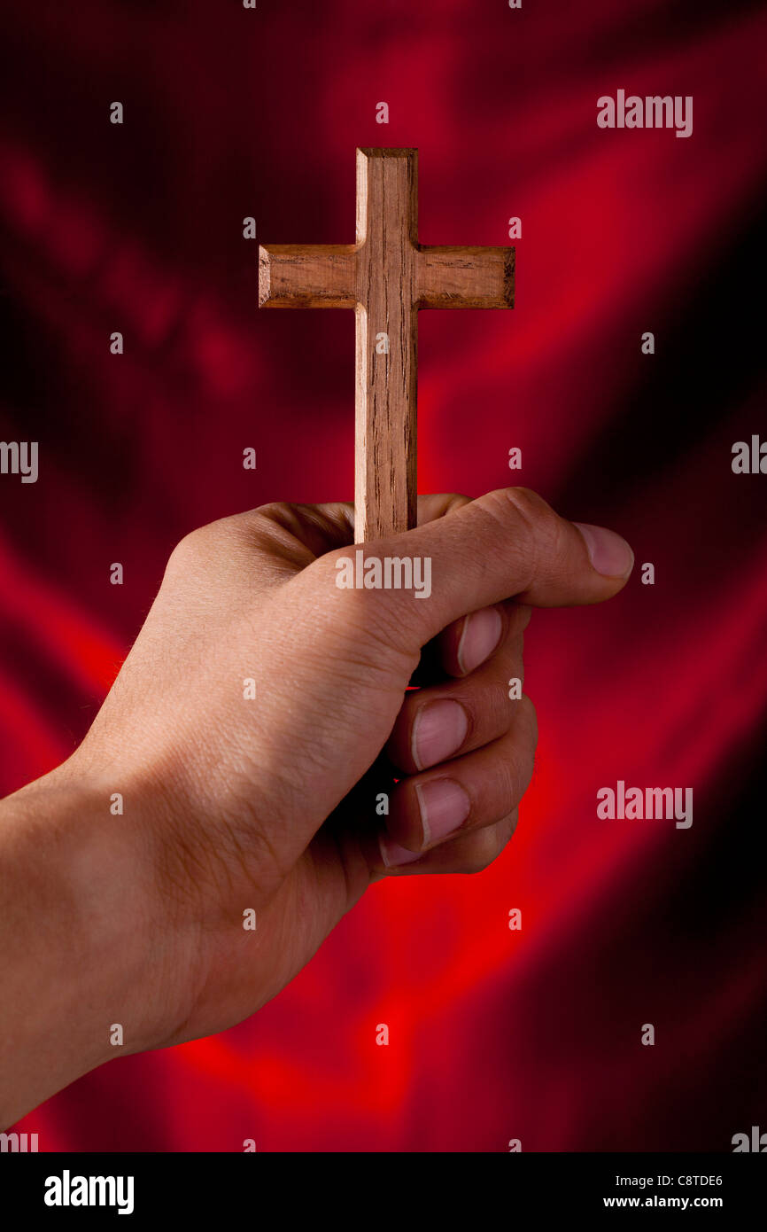 Human hand holding wooden cross over dark red background Stock Photo ...