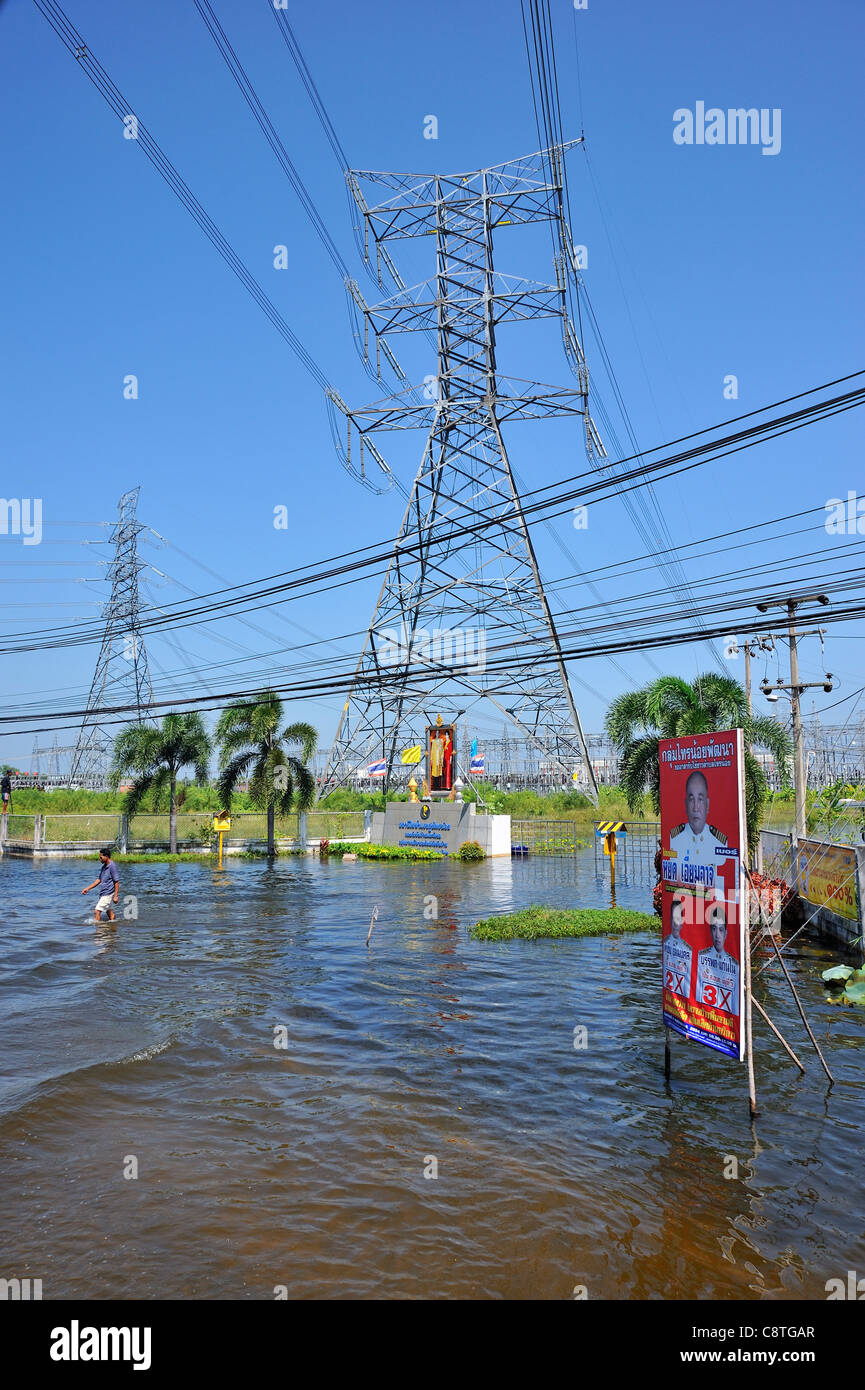 Thai man walking through floods in front of electrical substation ...