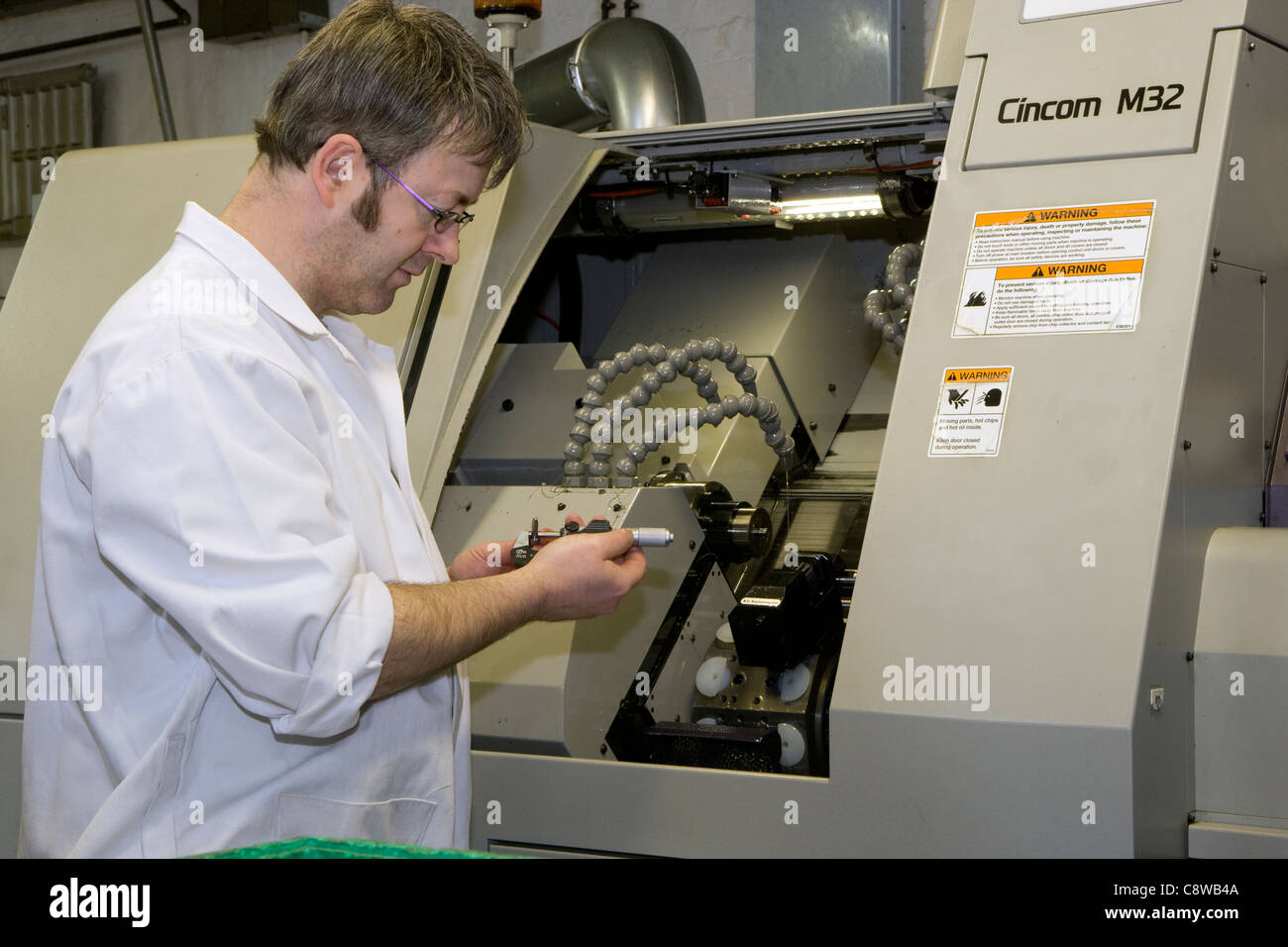 CNC lathe operator checking accuracy of a job with a micrometer Stock ...