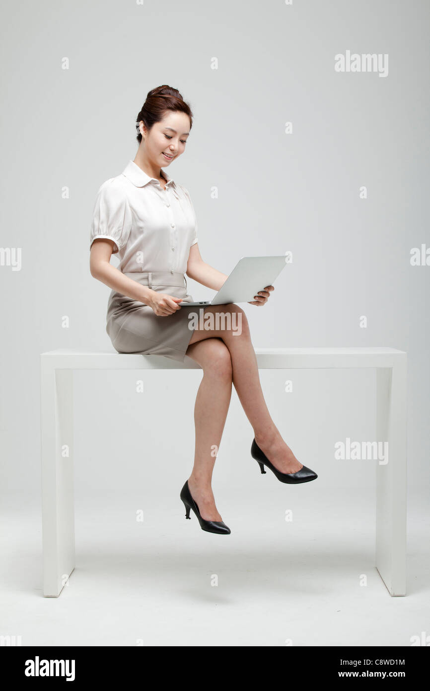 Asian Businesswoman Sitting On Desk Using Laptop Stock Photo - Alamy
