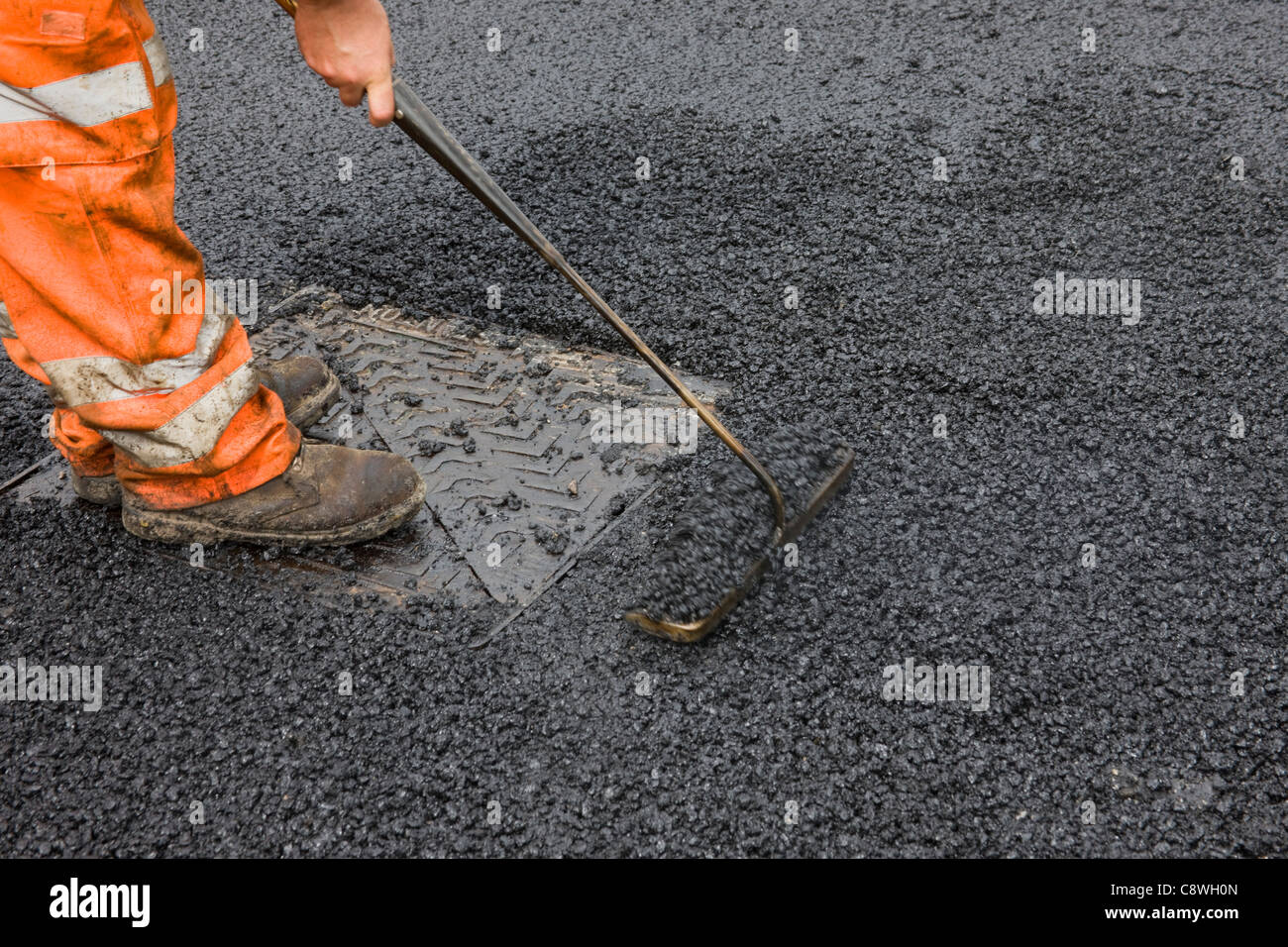 Asphalt being raked around a manhole cover to fill gaps in surface, of ...