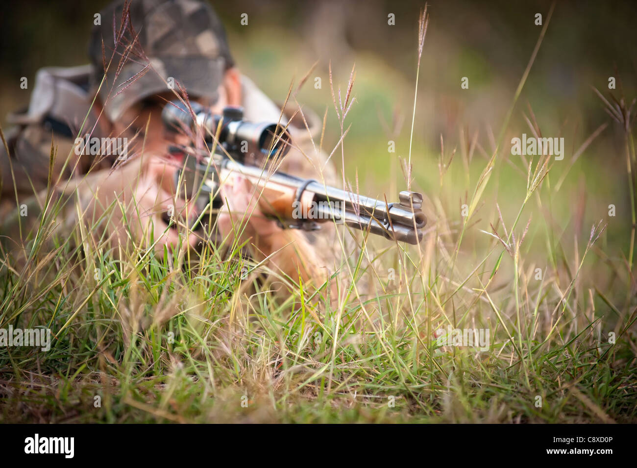 Camouflaged hunter lying in the grass pointing gun at hunting target ...