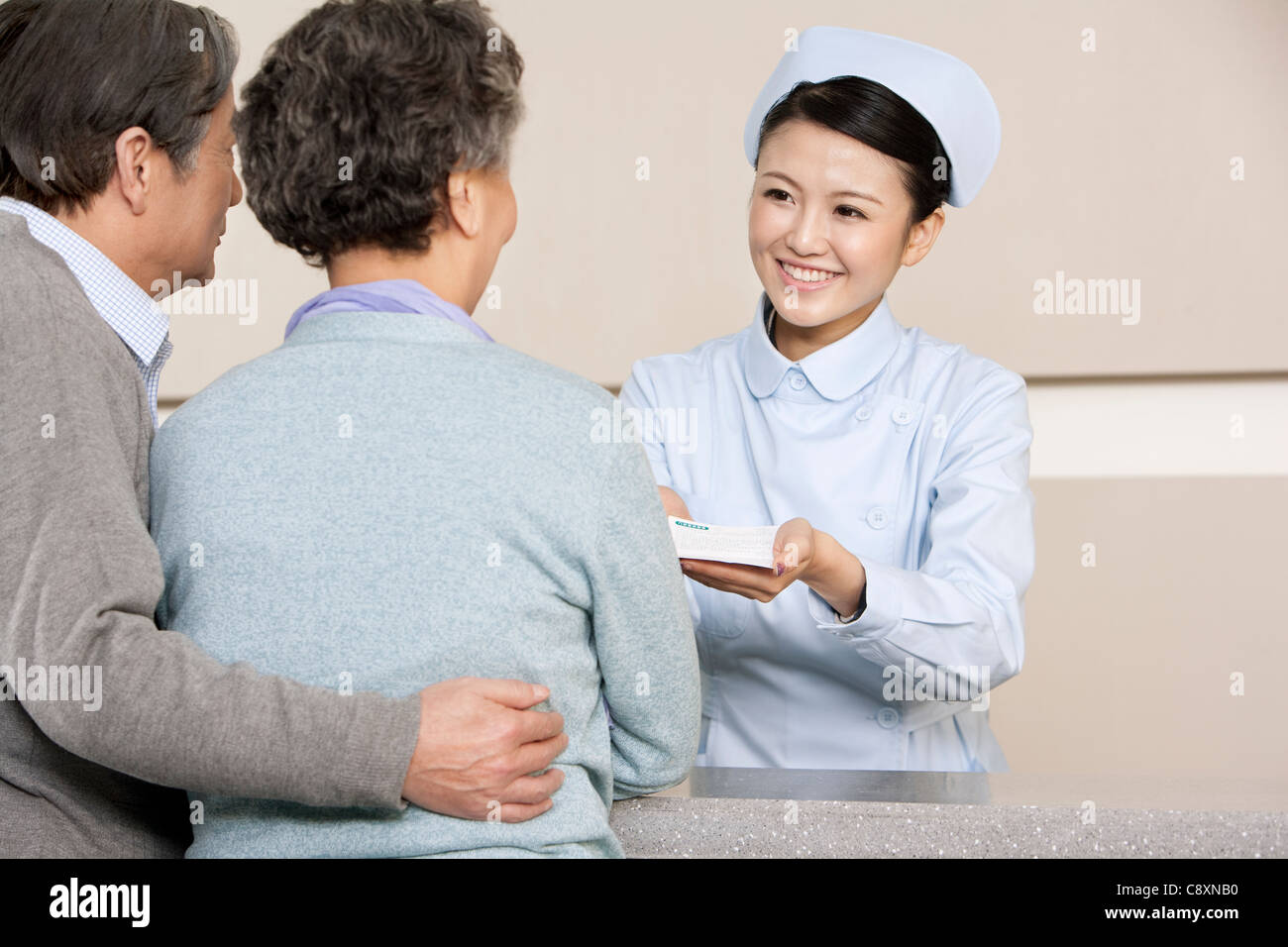 Young Nurse Helping Senior Couple at Nurses' Station Stock Photo - Alamy