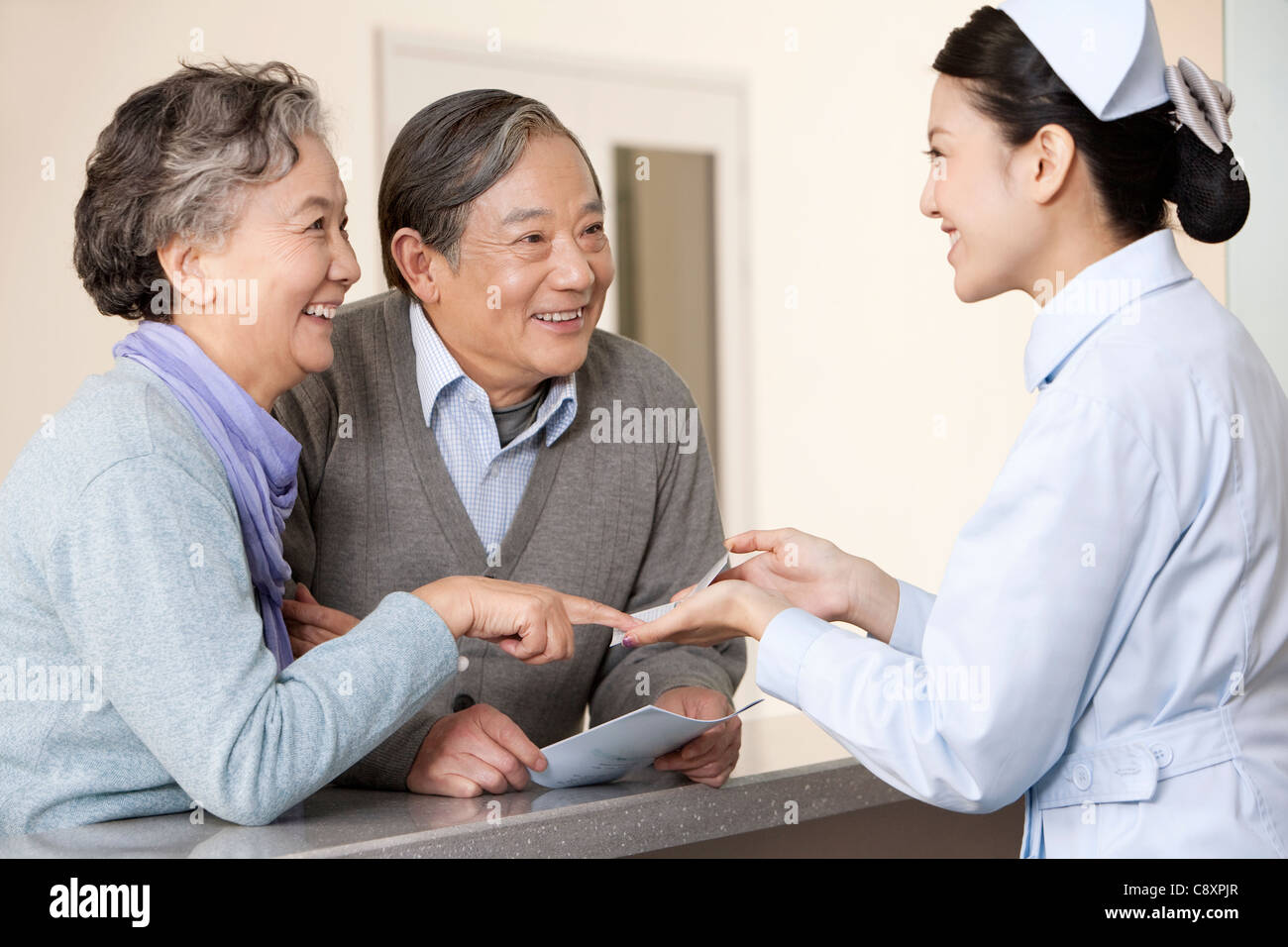 Young Nurse Helping Senior Couple at Nurses' Station Stock Photo - Alamy
