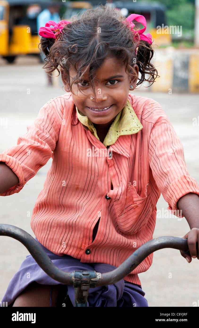 Poor Indian gypsy girl smiling with pink ribbons in her hair riding a ...
