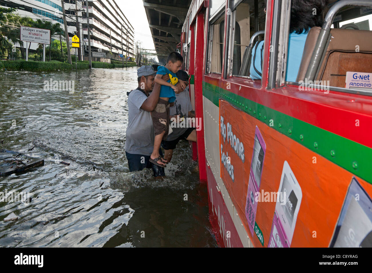 Passengers getting on a bus through flood water in Bangkok city centre ...
