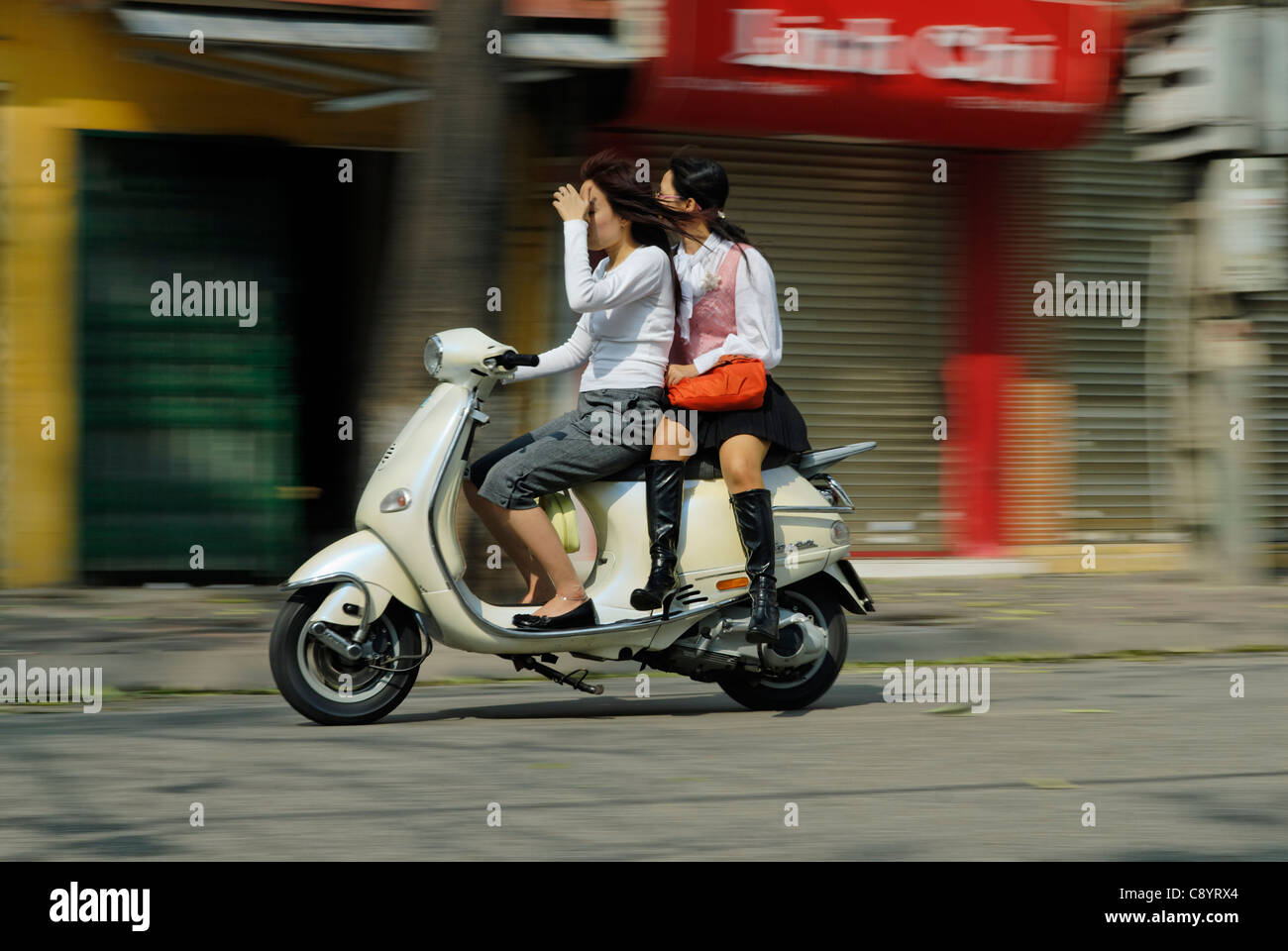 Asia, Vietnam, Hanoi. Hanoi old quarter. Two women on Vespa motorbike rushing through Hanoi ...
