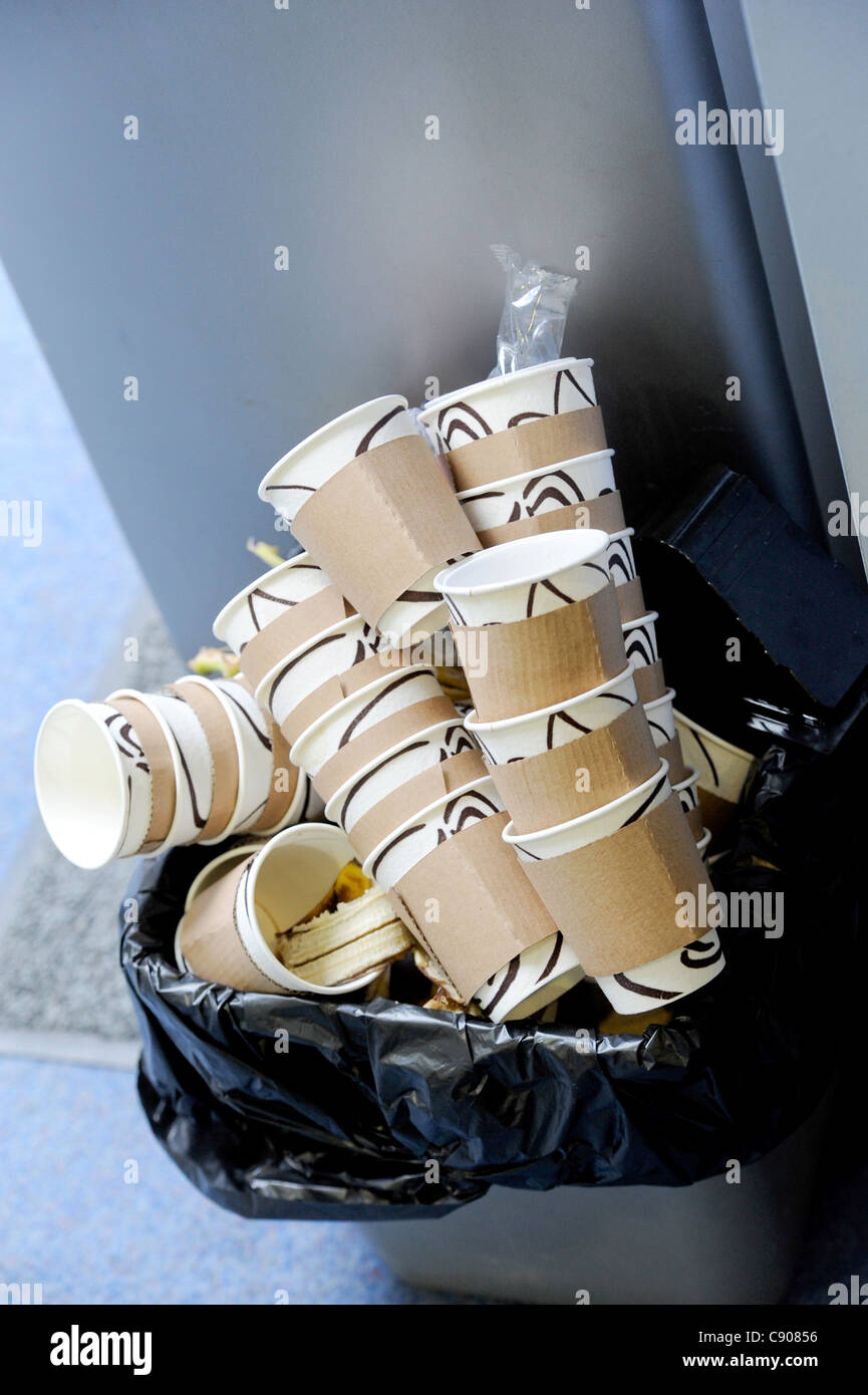 A stack of empty disposable coffee cups spilling out of a rubbish bin ...
