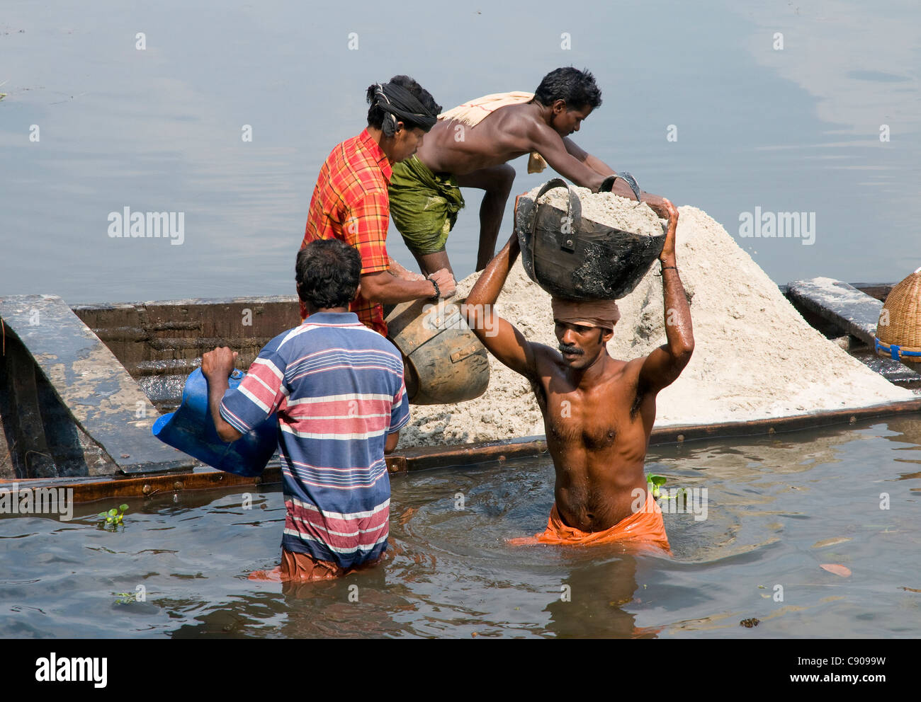 Men manhandling building materials ashore from a vallam(a traditional ...