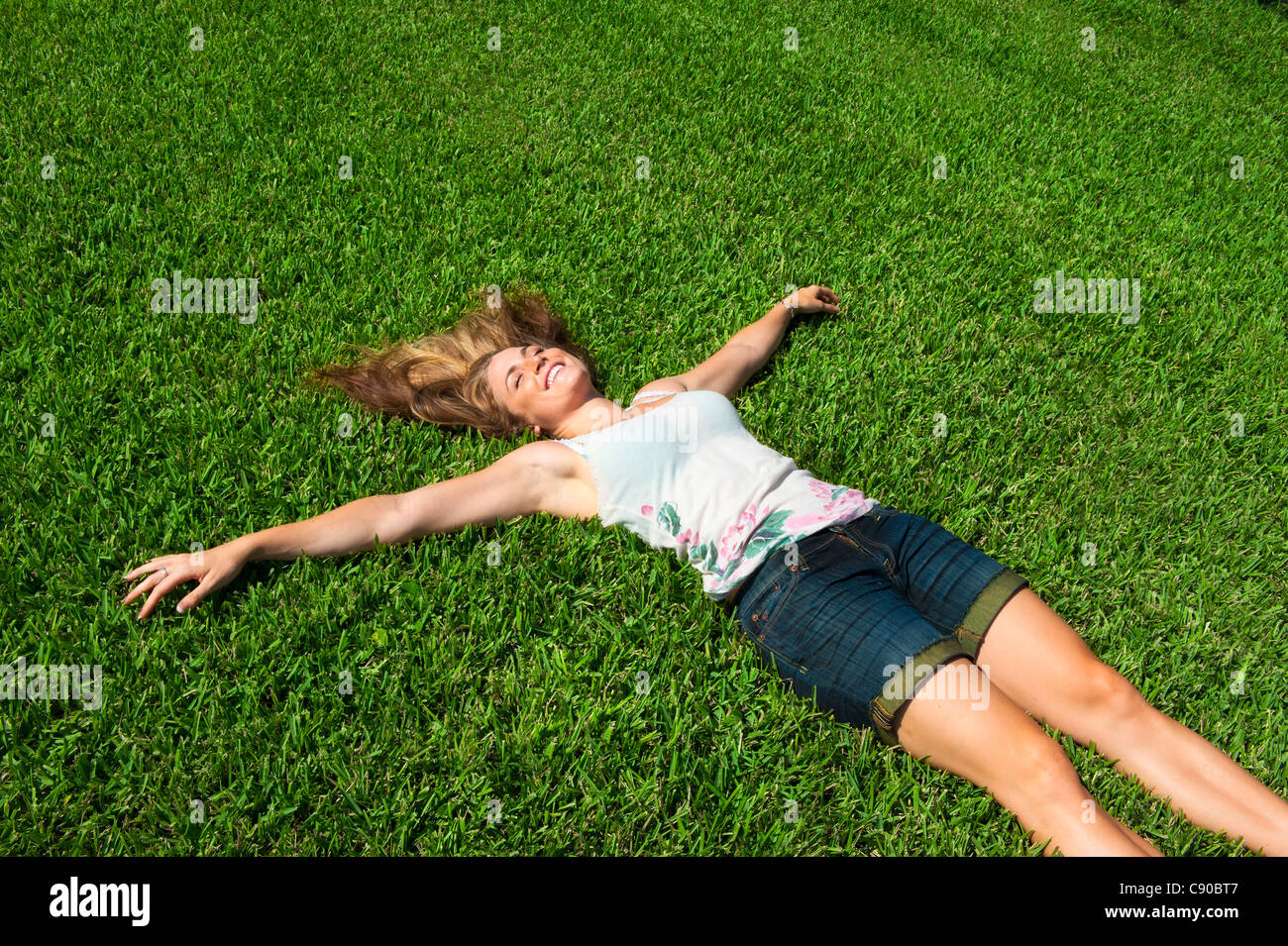 Young woman 20s lying on her back on perfect green grass in the ...