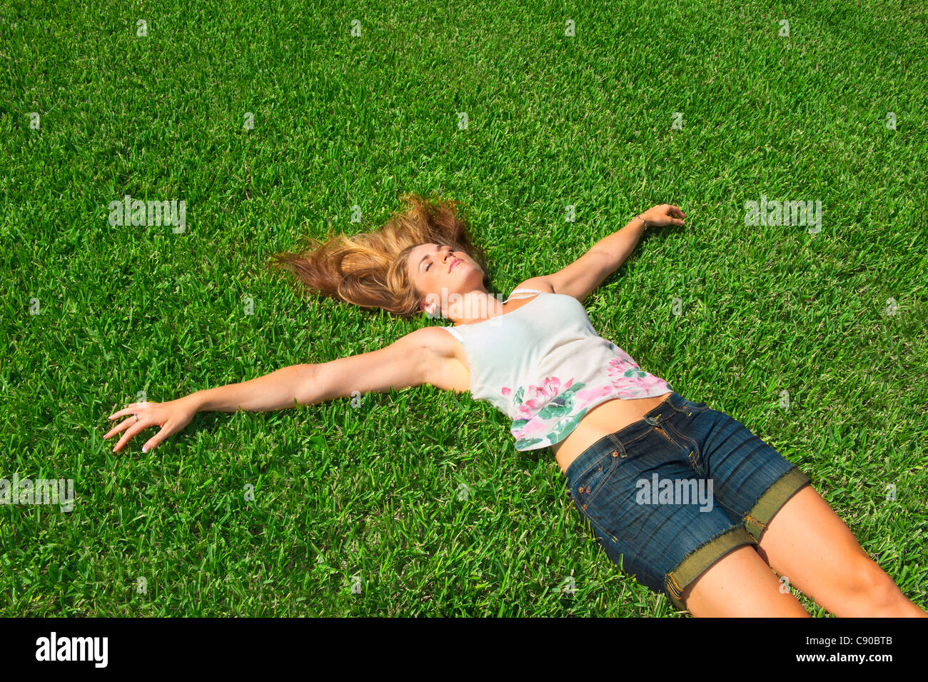 Young woman 20s lying on her back on the perfect green grass in the sun ...