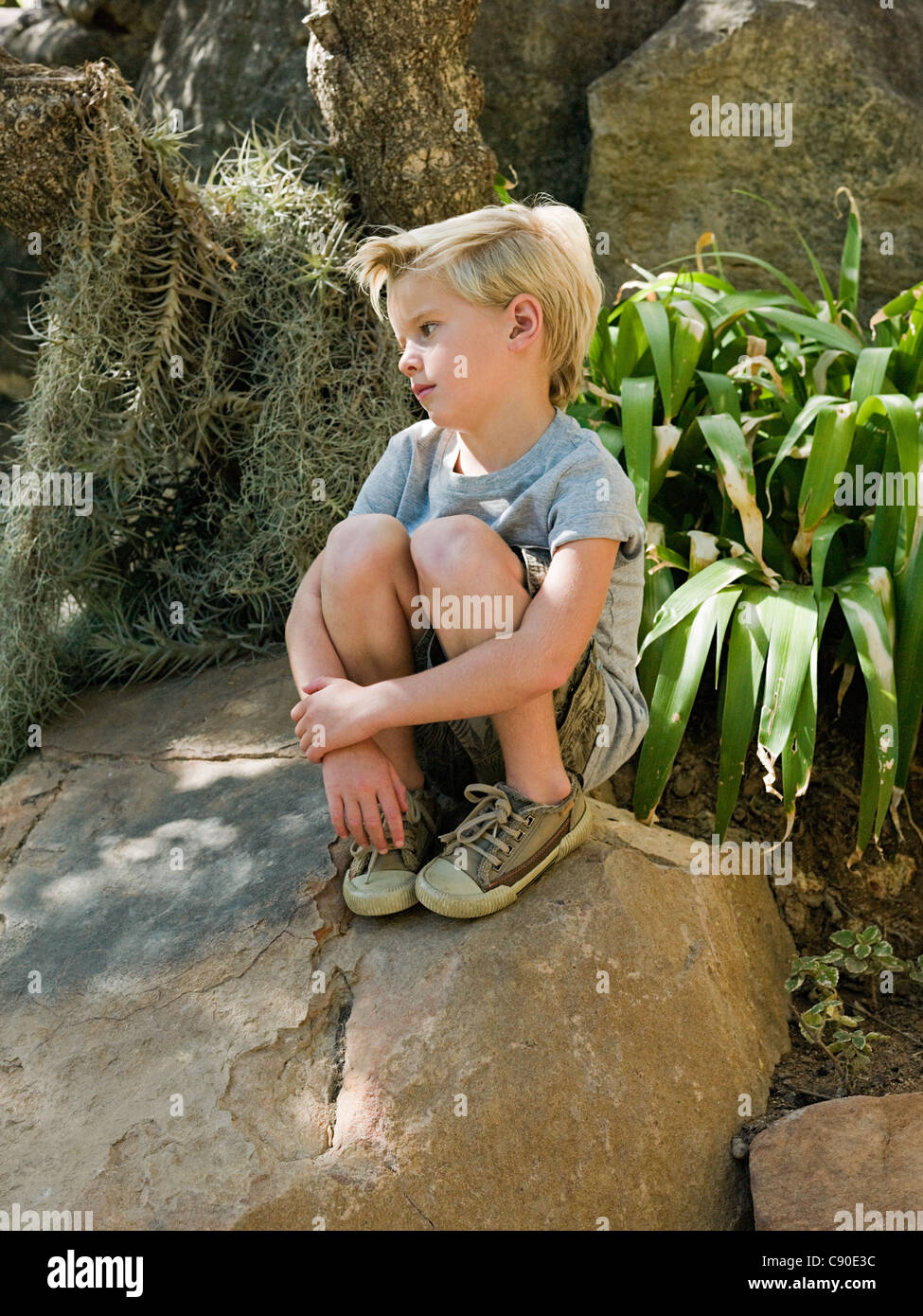 Pensive boy sitting on rock Stock Photo - Alamy