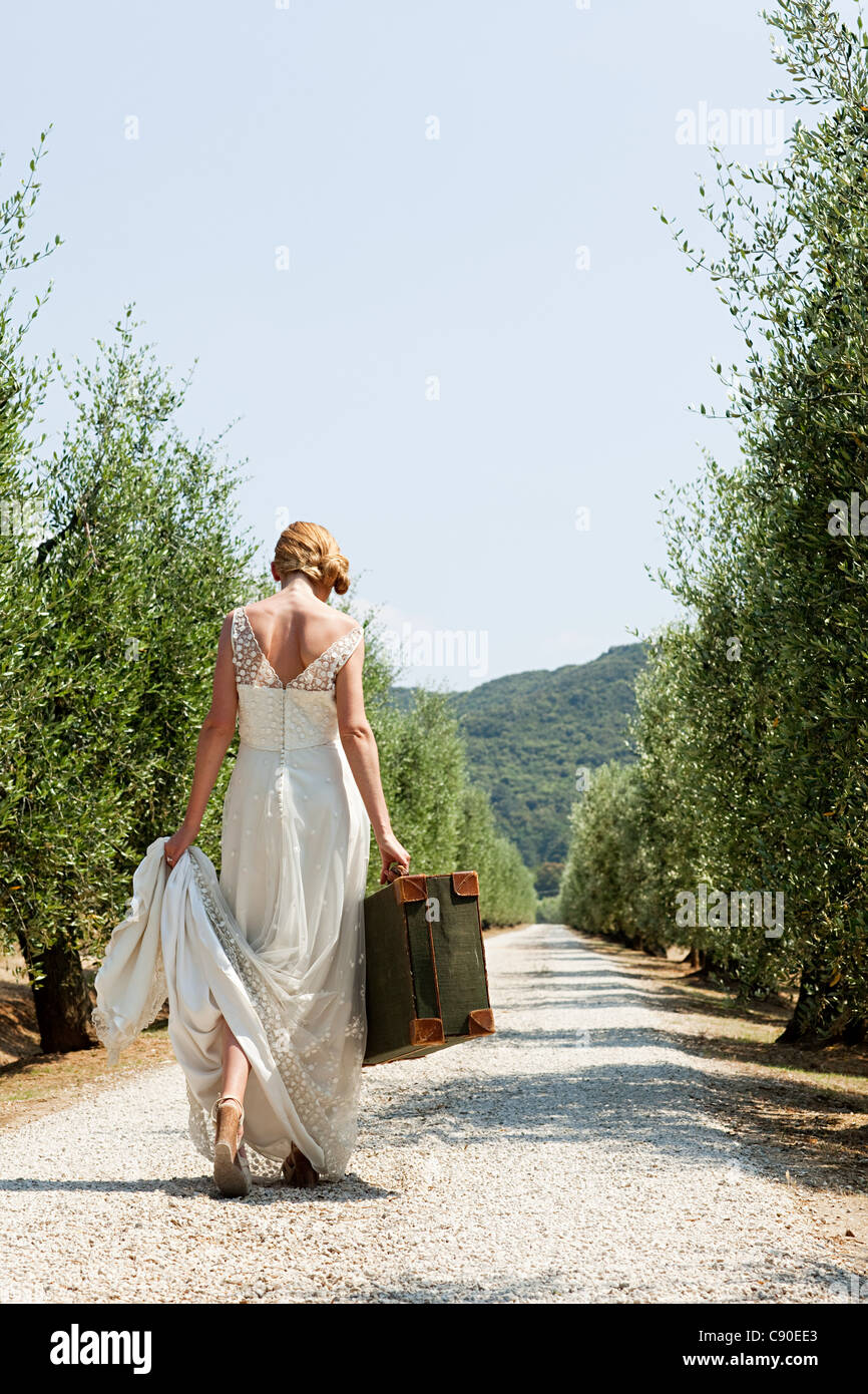 Bride carrying suitcase on country road Stock Photo - Alamy