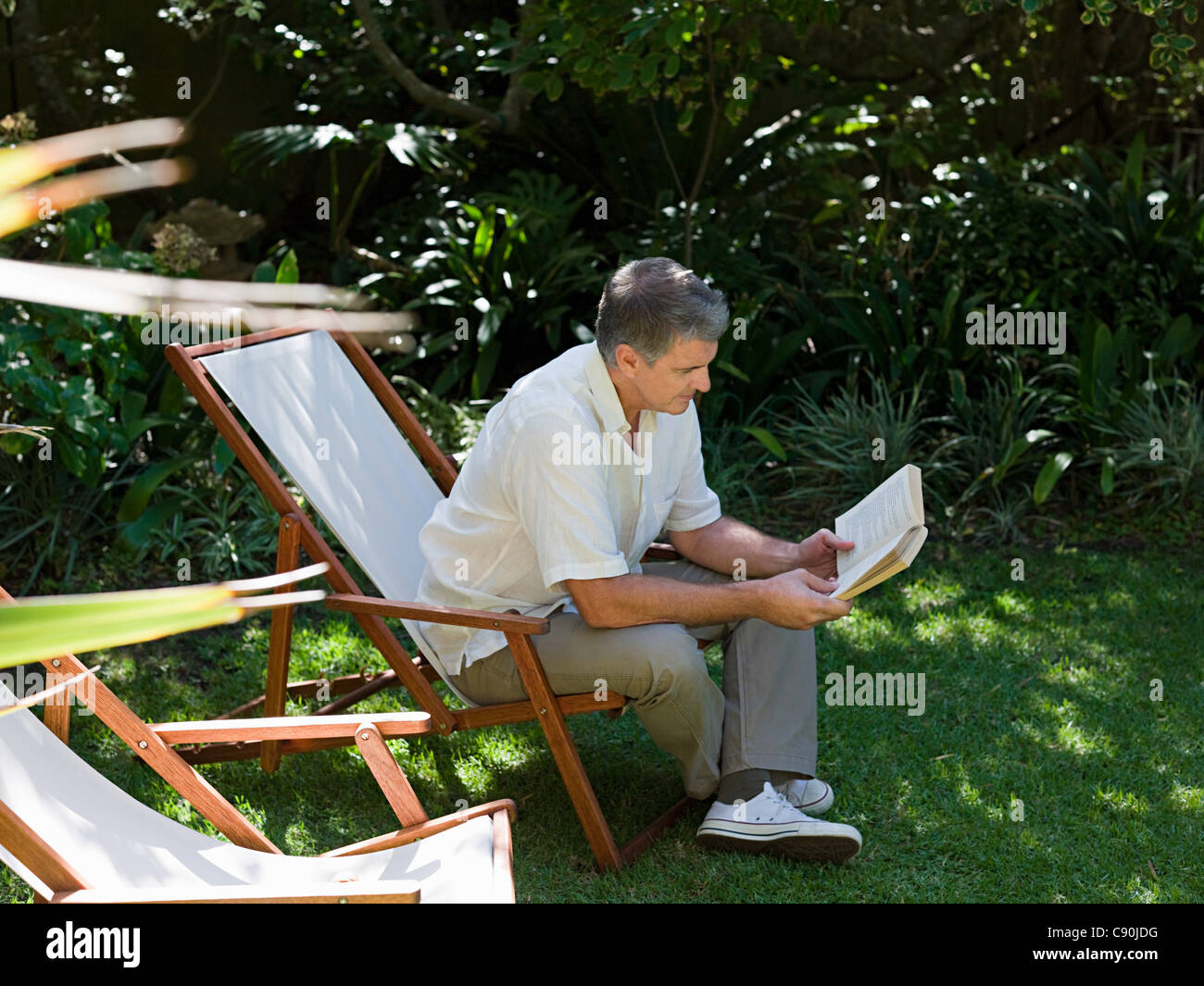 Man sitting on deckchair in garden reading book Stock Photo - Alamy