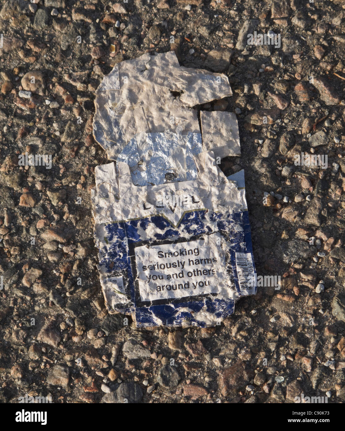 Worn empty Level cigarette packet on the ground. Warning text in ...