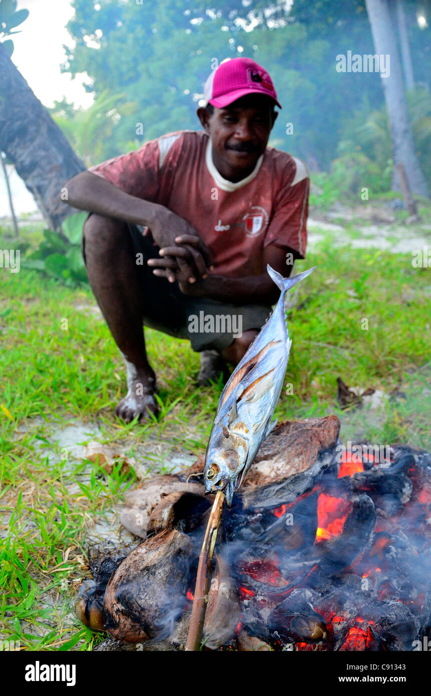 Indonesian fisherman roasting fish over fire, Raja Ampat islands near ...