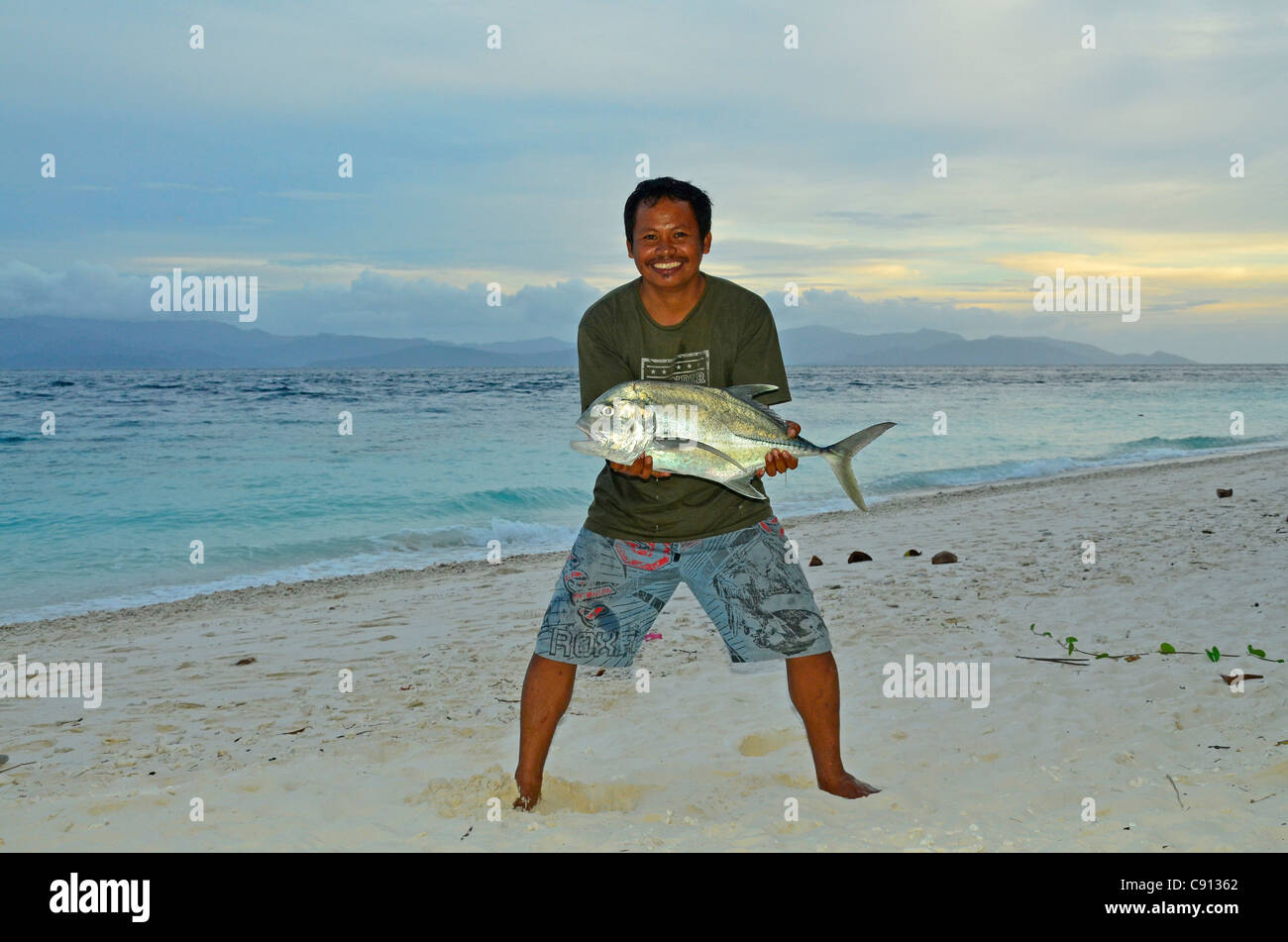Excited fisherman showing big fish on beach, Raja Ampat islands near ...