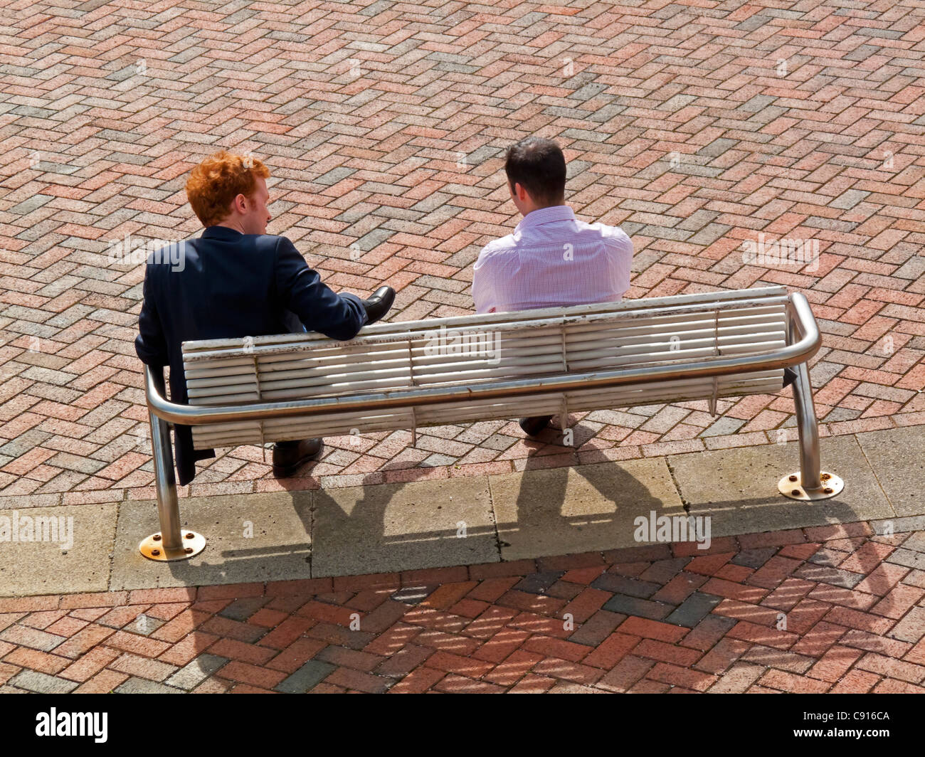 Two male office workers sitting on a metal bench in Manchester England ...