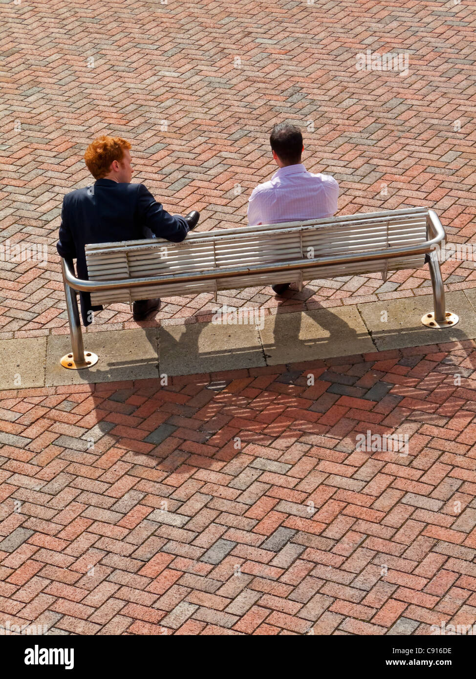 Two male office workers sitting on a metal bench in Manchester England ...