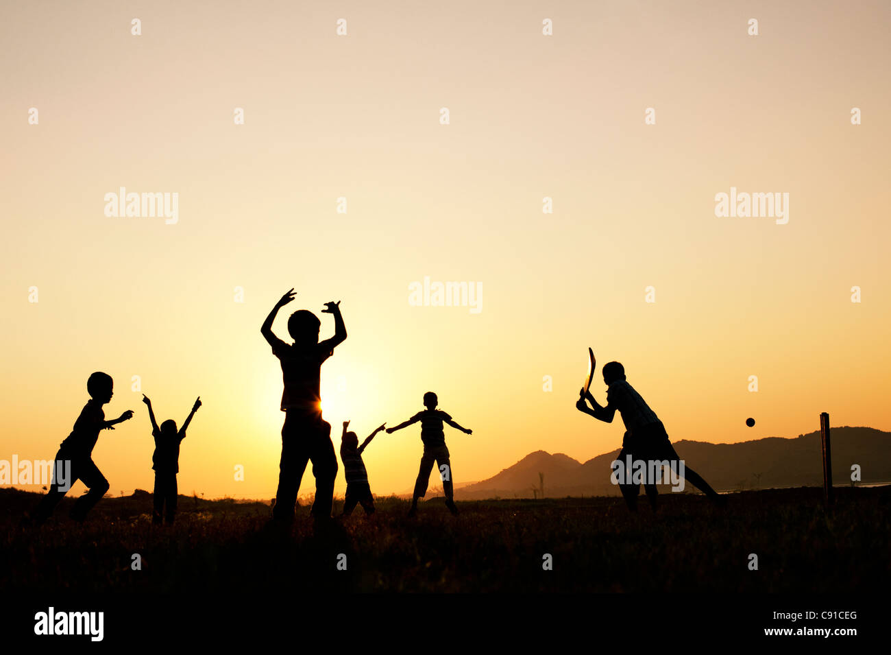 Silhouette of young Indian boys playing cricket against a sunset ...