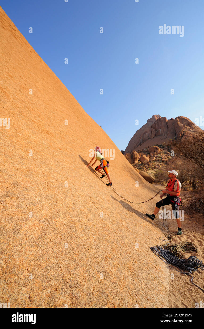Woman climbing at red rock face, man belaying, Great Spitzkoppe ...
