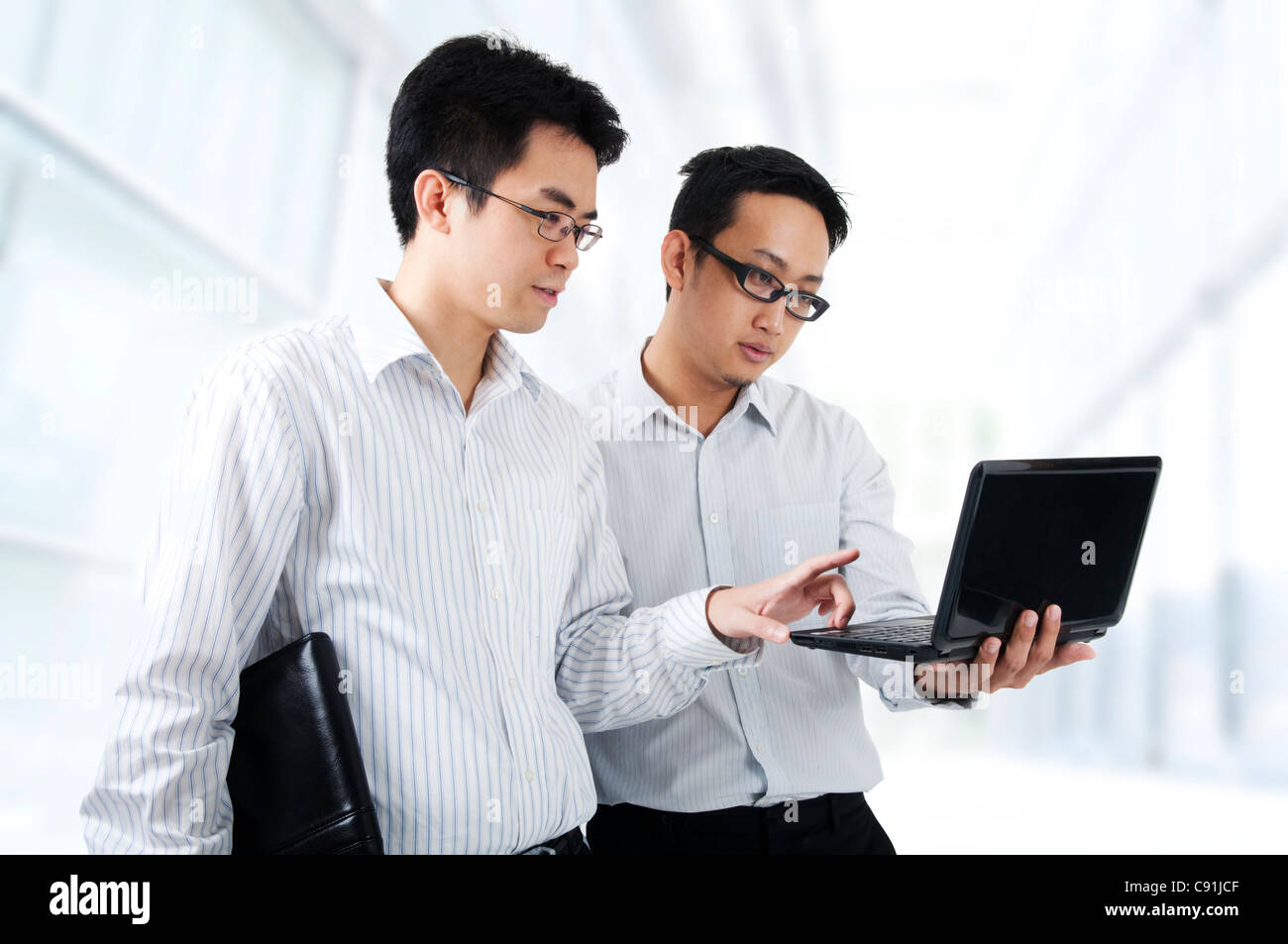 Two Asian young executives working on laptop, office building as ...