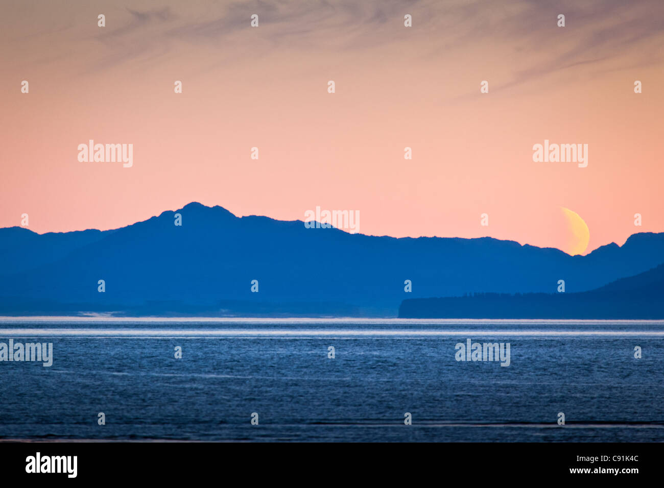 Scenic view at dawn of a crescent moon setting behind coastal mountains ...