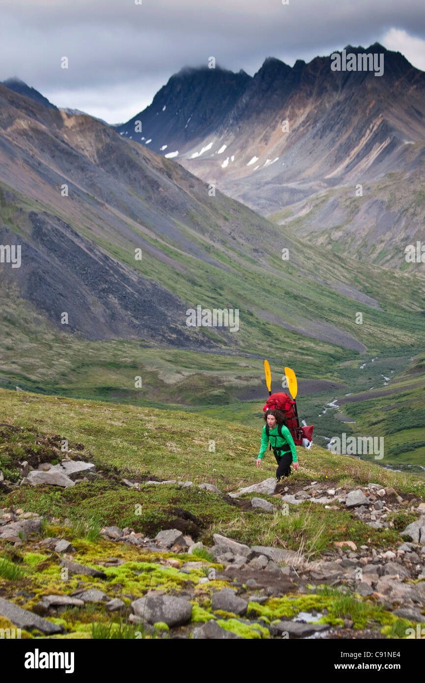 Woman with a packraft hiking upper Windy Creek to a mountain pass under ...