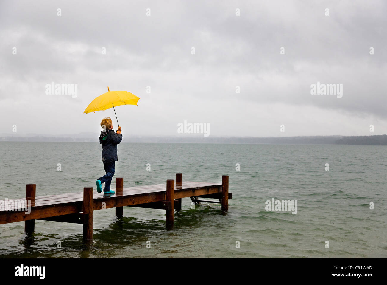 Boy carrying umbrella on wooden dock Stock Photo - Alamy
