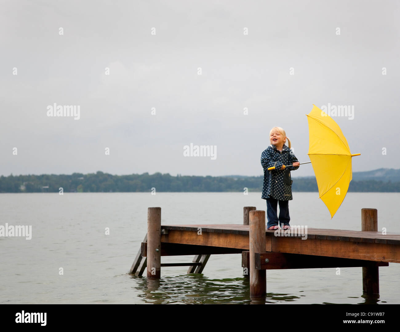 Girl holding yellow umbrella on dock Stock Photo - Alamy
