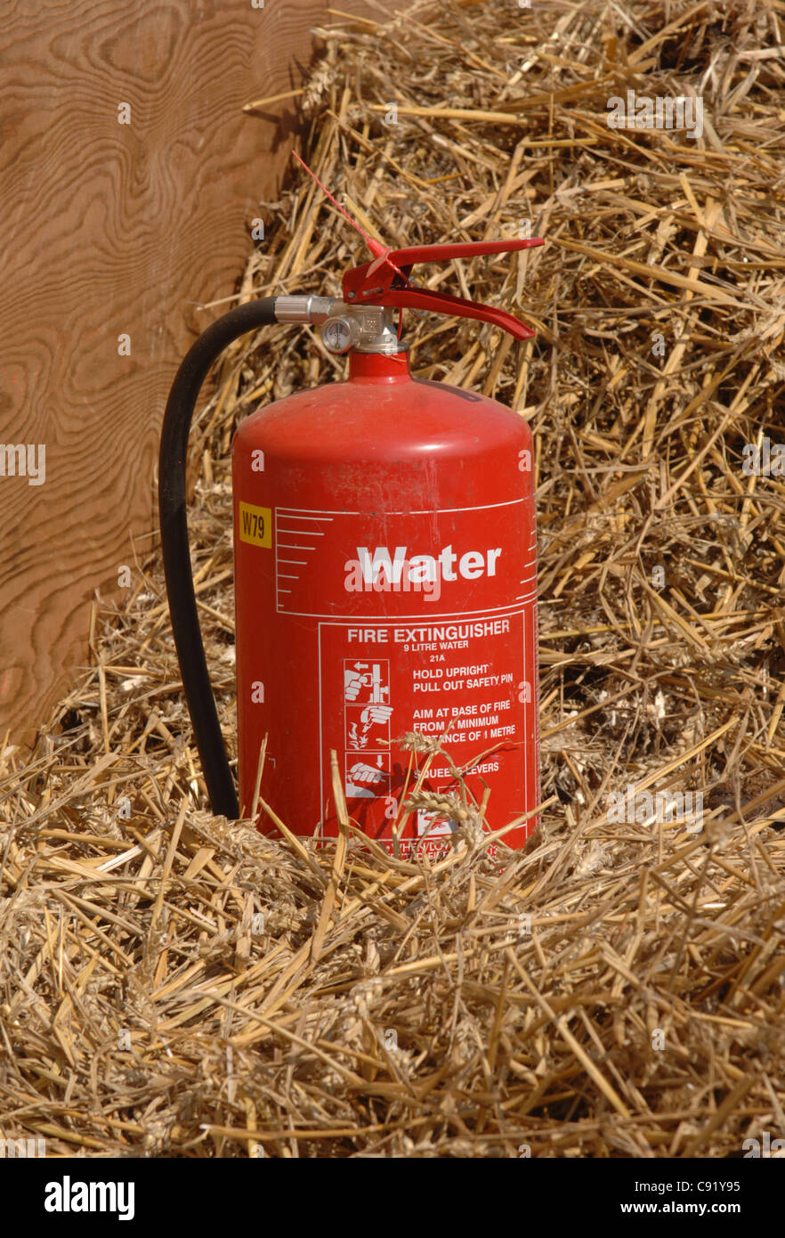 A red water fire extinguisher partially hidden in straw Stock Photo - Alamy