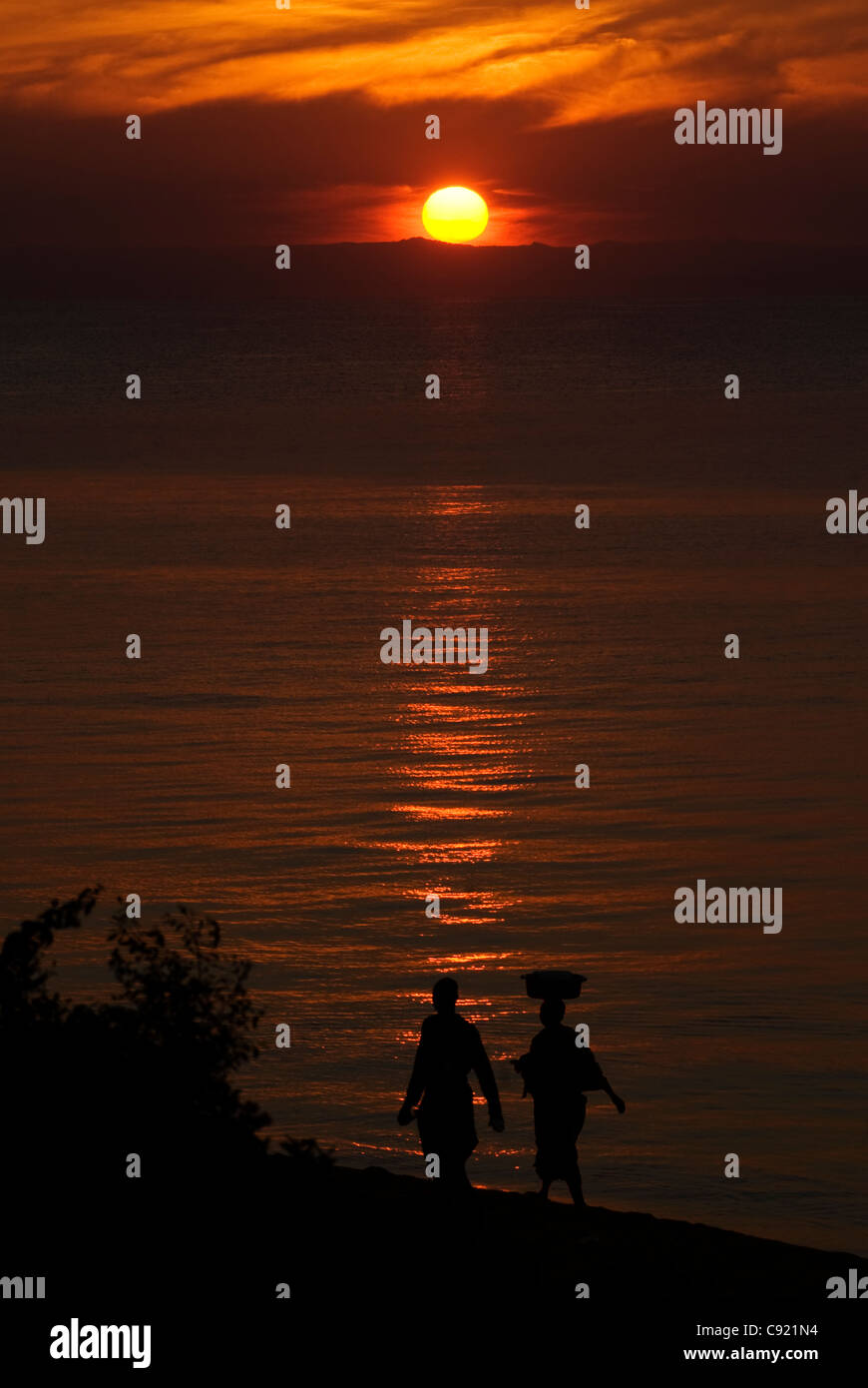 People walking along lakeshore as the sun rises over Lake Malawi at ...