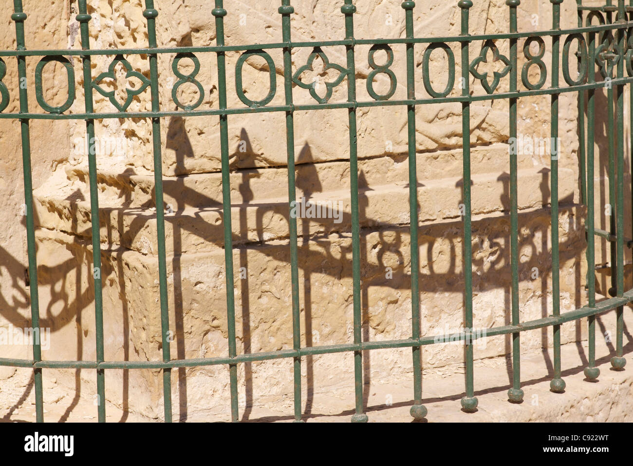 Ornate painted wrought iron railings casting a shadow on the limestone ...