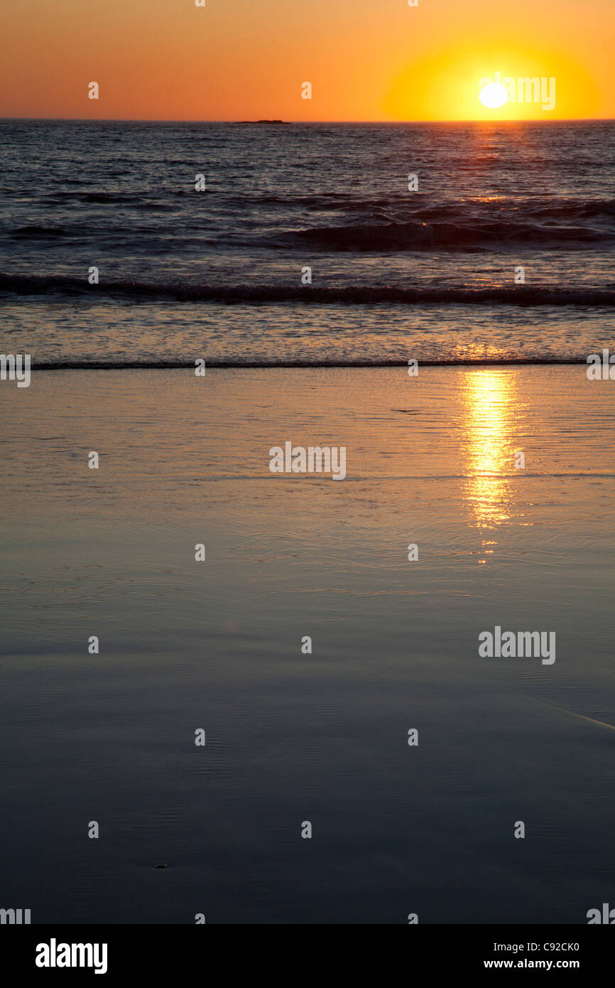 Sun setting over ocean on beach Stock Photo - Alamy