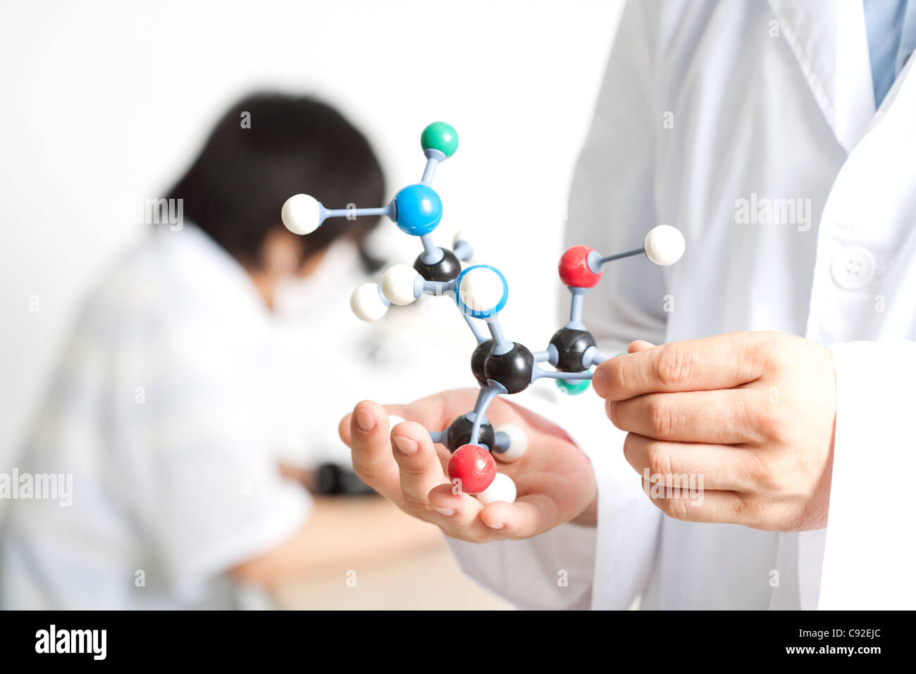 Close-up of man holding molecules with man working in the background ...