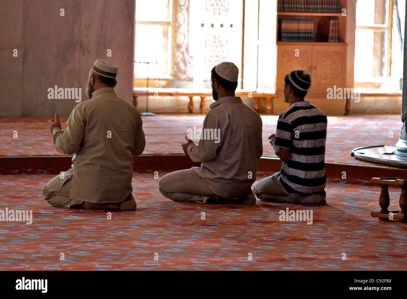Three men without shoes and wearing skull caps taqiyah worshiping ...