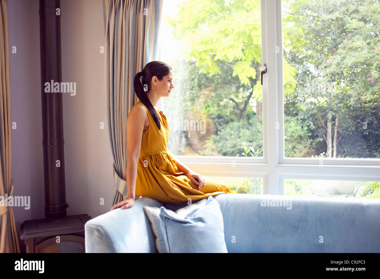 Woman sitting by window indoors Stock Photo - Alamy