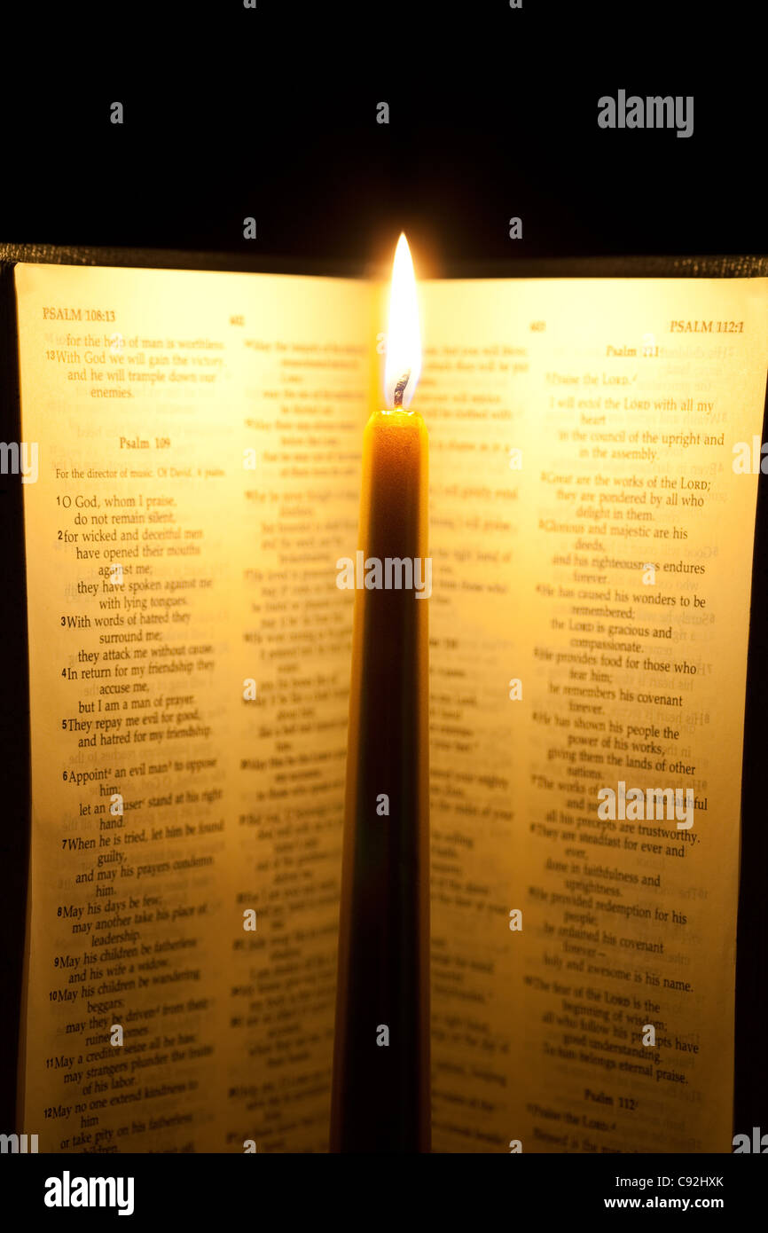 An open bible with illuminated candle in between Stock Photo - Alamy