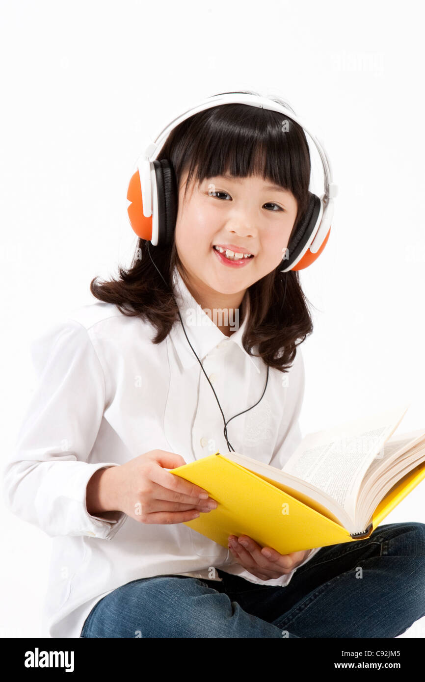 A girl wearing headphone with reading book, smiling Stock Photo - Alamy