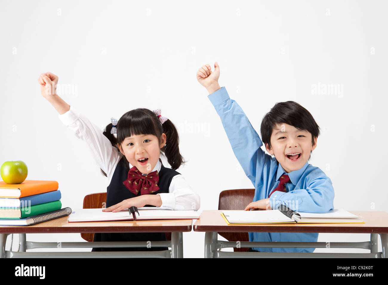 Boy and girl sitting on school bench with hands raised Stock Photo - Alamy