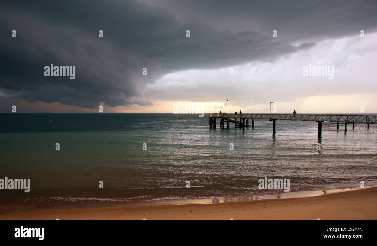 Huge black storm clouds gather as silhouetted people fish off a pier ...