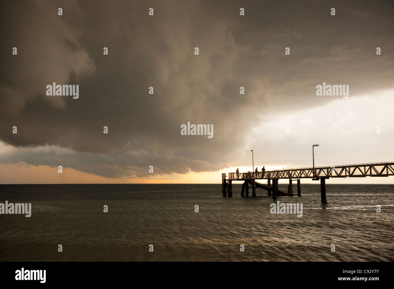 Huge black storm clouds gather as silhouetted people fish off a pier ...